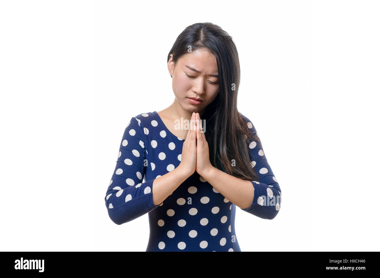 Young Chinese woman praying with clasped hands and her eyes closed in a ...