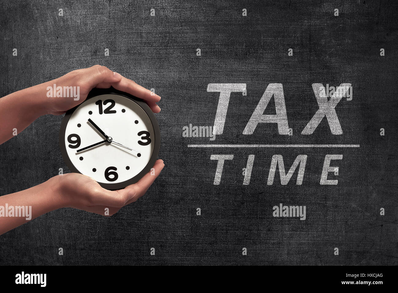 People hand holding black alarm clock beside Tax time announcement on ...