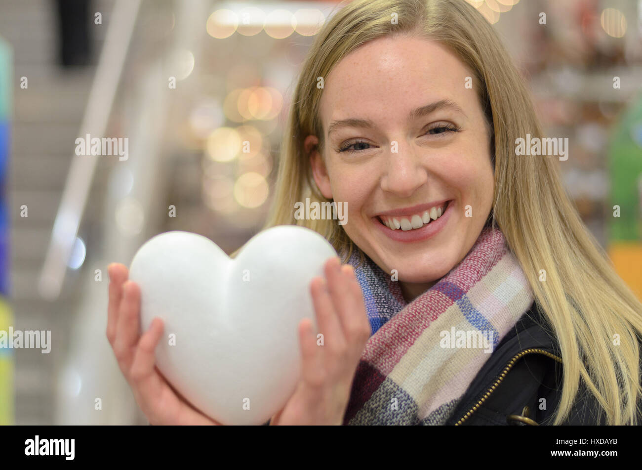 Happy young woman holding a large white heart in her hands as she gives ...