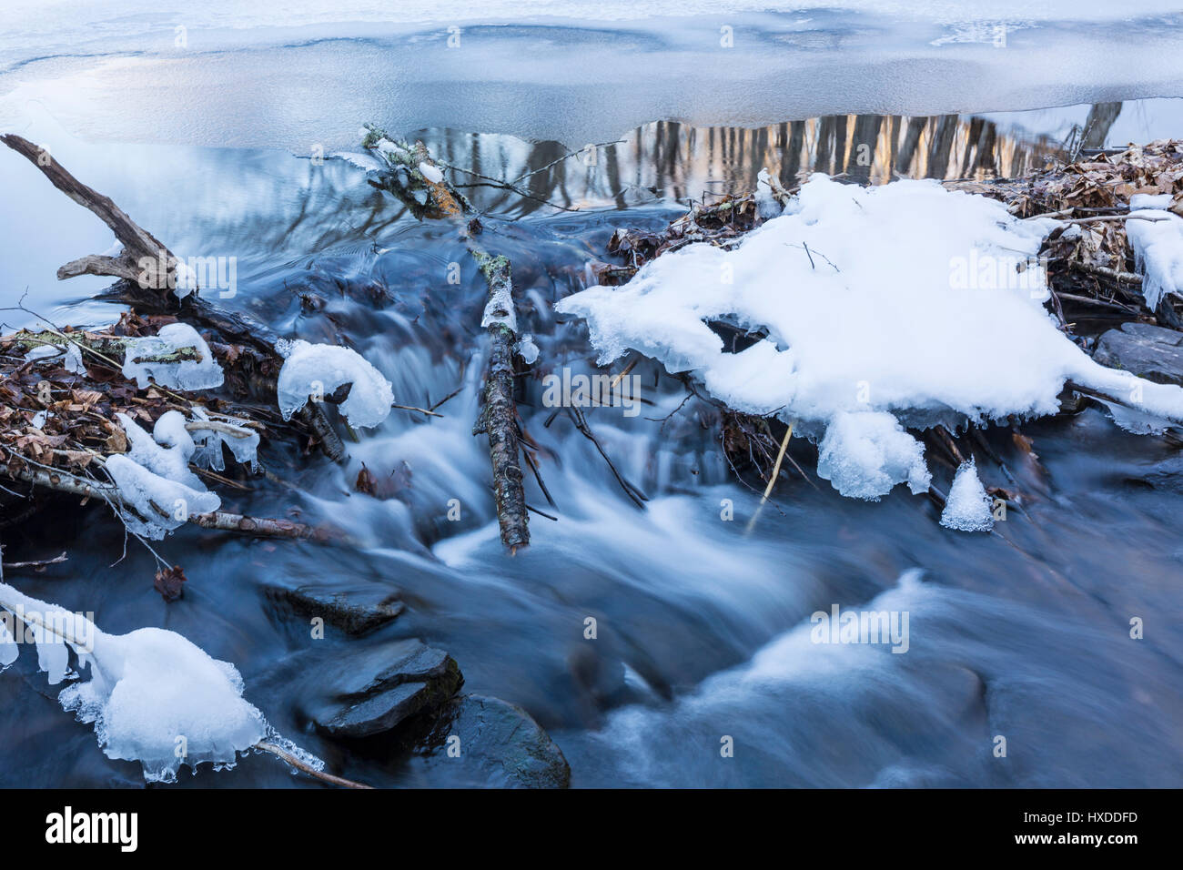Reflections and ripples in the water that flows out of partially frozen ...