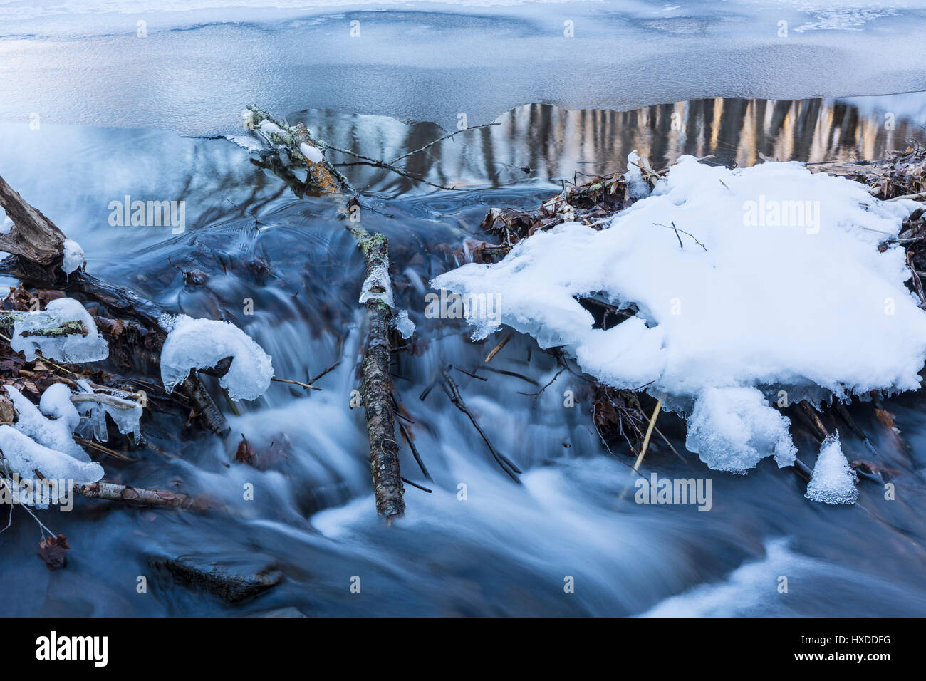 Reflections and ripples in the water that flows out of partially frozen ...