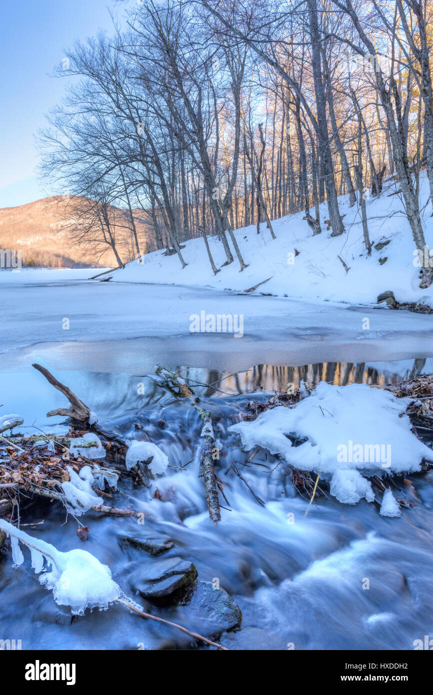 Reflections and ripples in the water that flows out of partially frozen ...