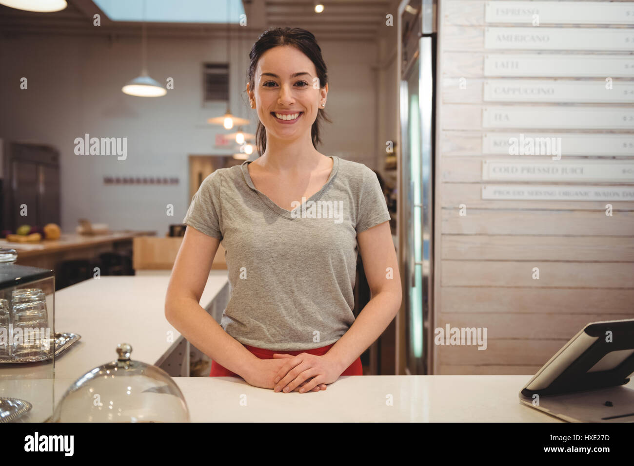 Portrait of smiling female barista standing at counter in coffee shop ...