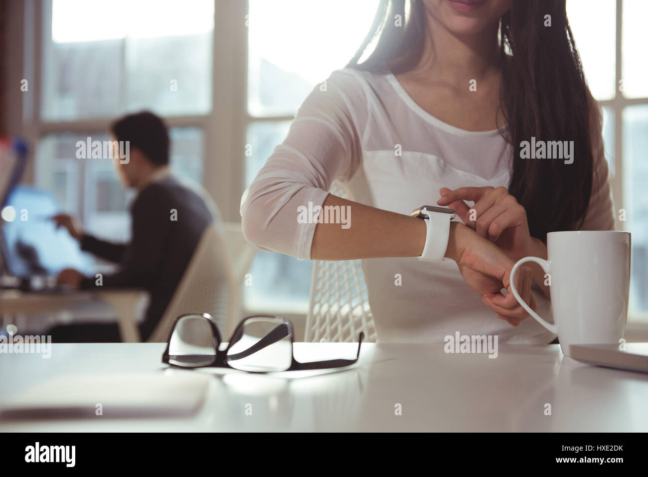 Female executive using smartwatch at desk in office Stock Photo - Alamy