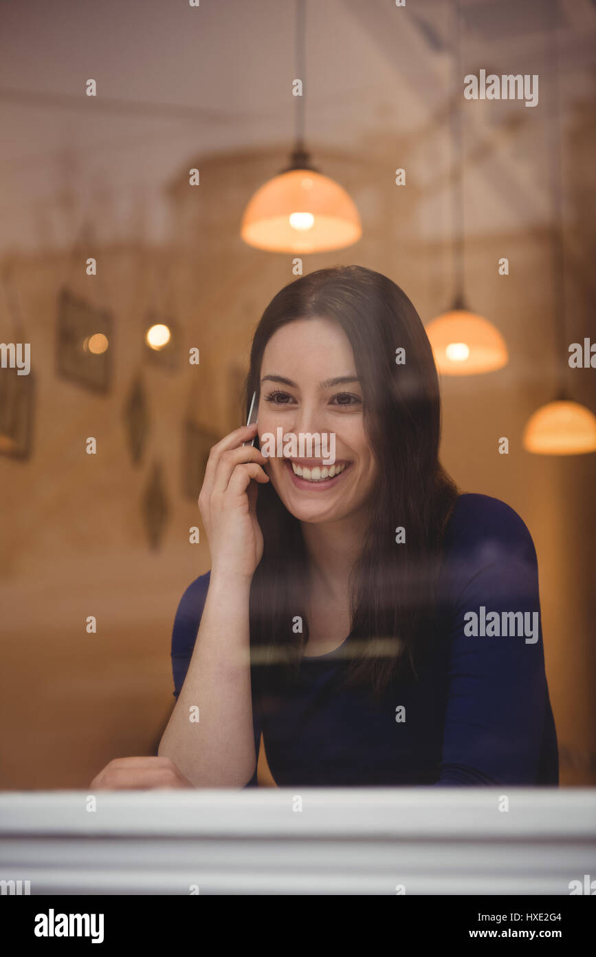 Smiling young woman talking on phone at coffee shop seen through window ...
