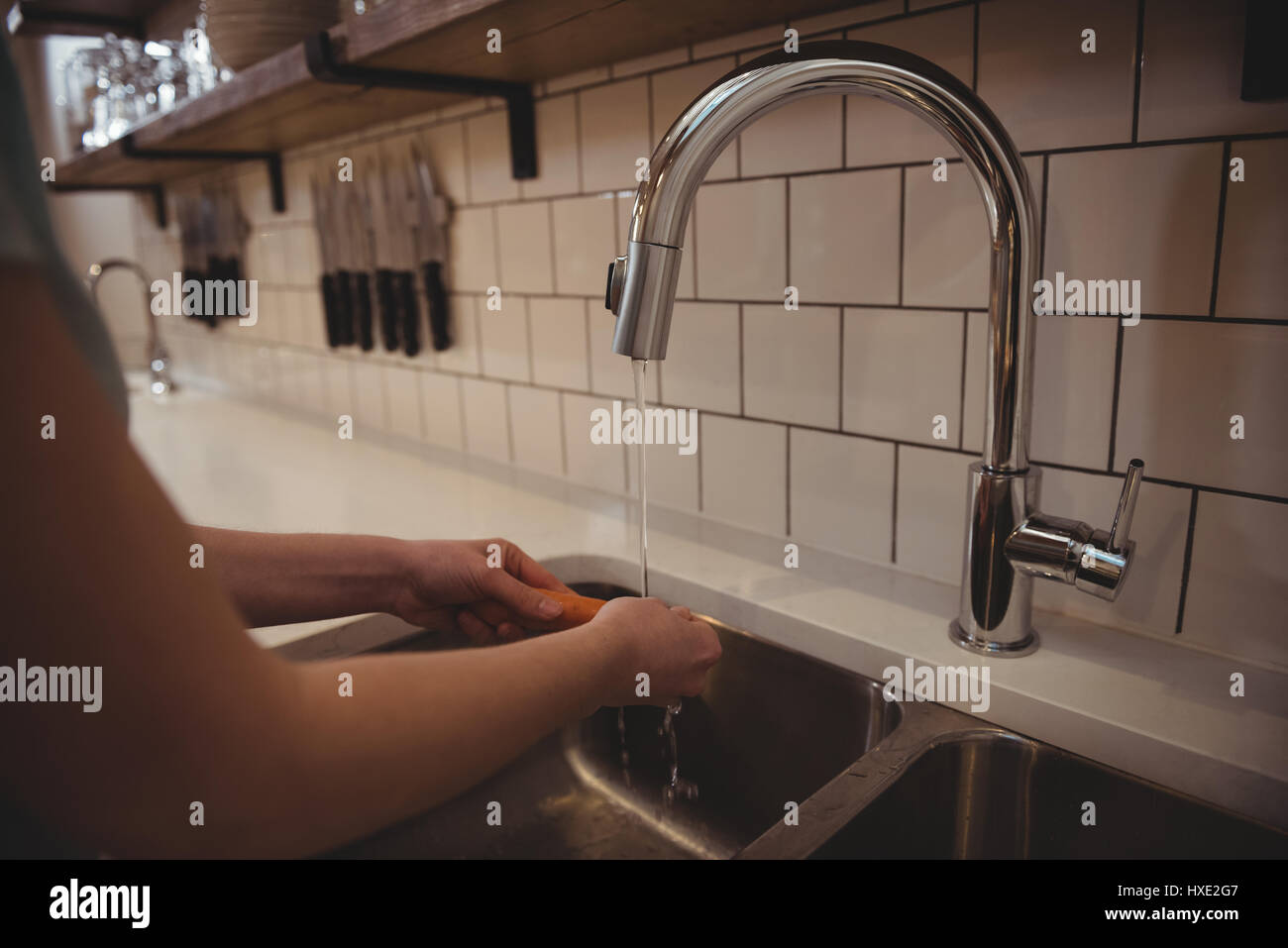 Close-up of female chef washing carrot under the tap in commercial ...