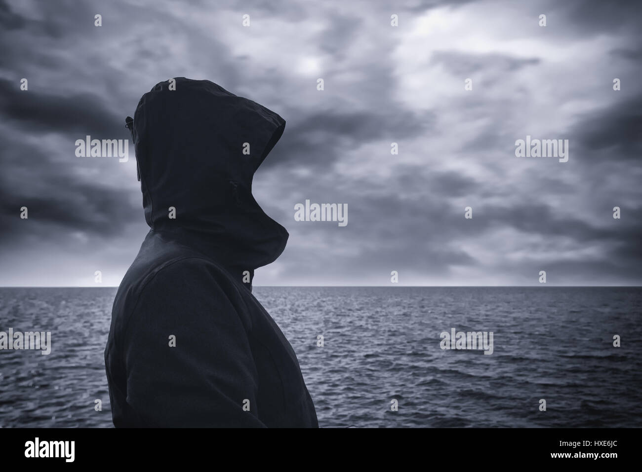 Faceless hooded person looking into distance at horizon over the sea ...