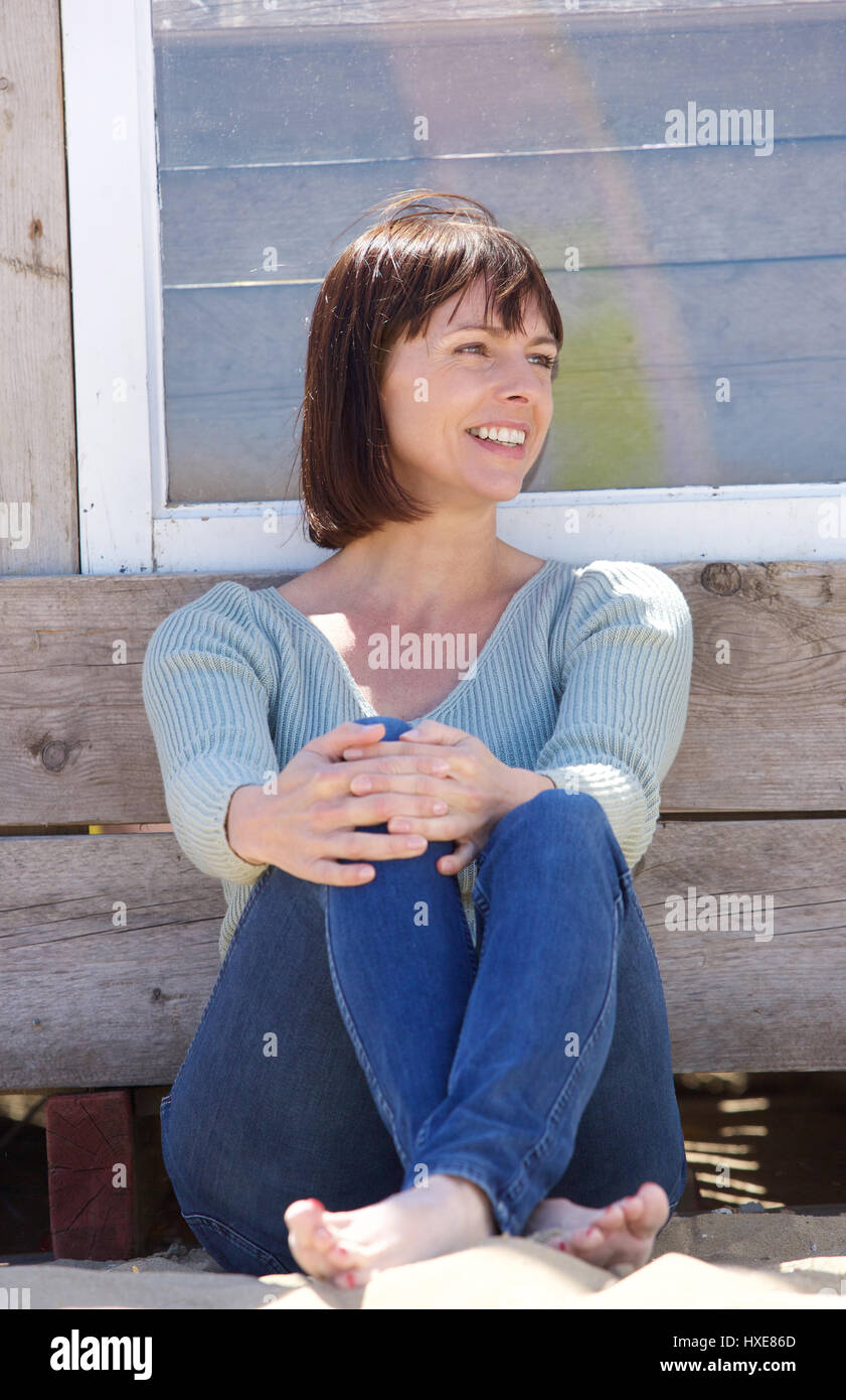 Portrait of a happy middle aged woman in jeans sitting outside Stock ...