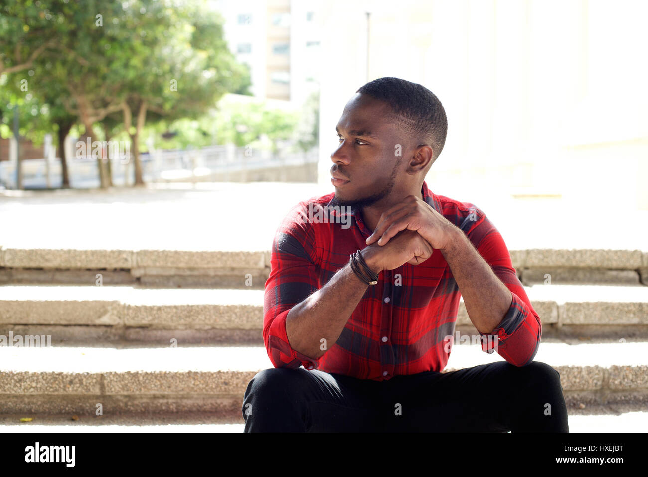 Close up portrait of pensive young african man sitting outdoors on ...