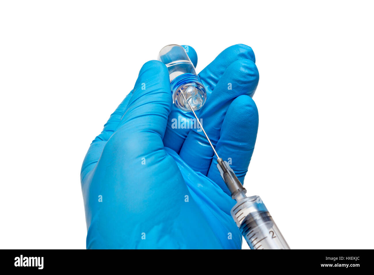 Medical gloved hand holding syringe with a bead of liquid emerging ...