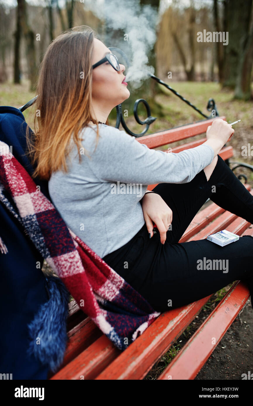 Young girl smoking cigarette outdoors sitting on bench. Concept of ...