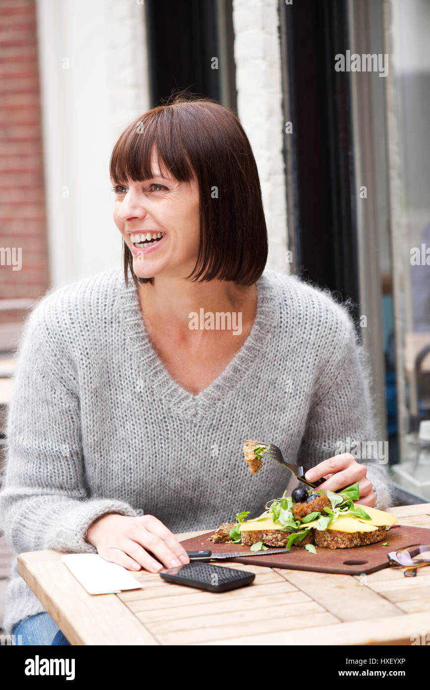 Portrait of a smiling woman sitting at table eating food Stock Photo ...