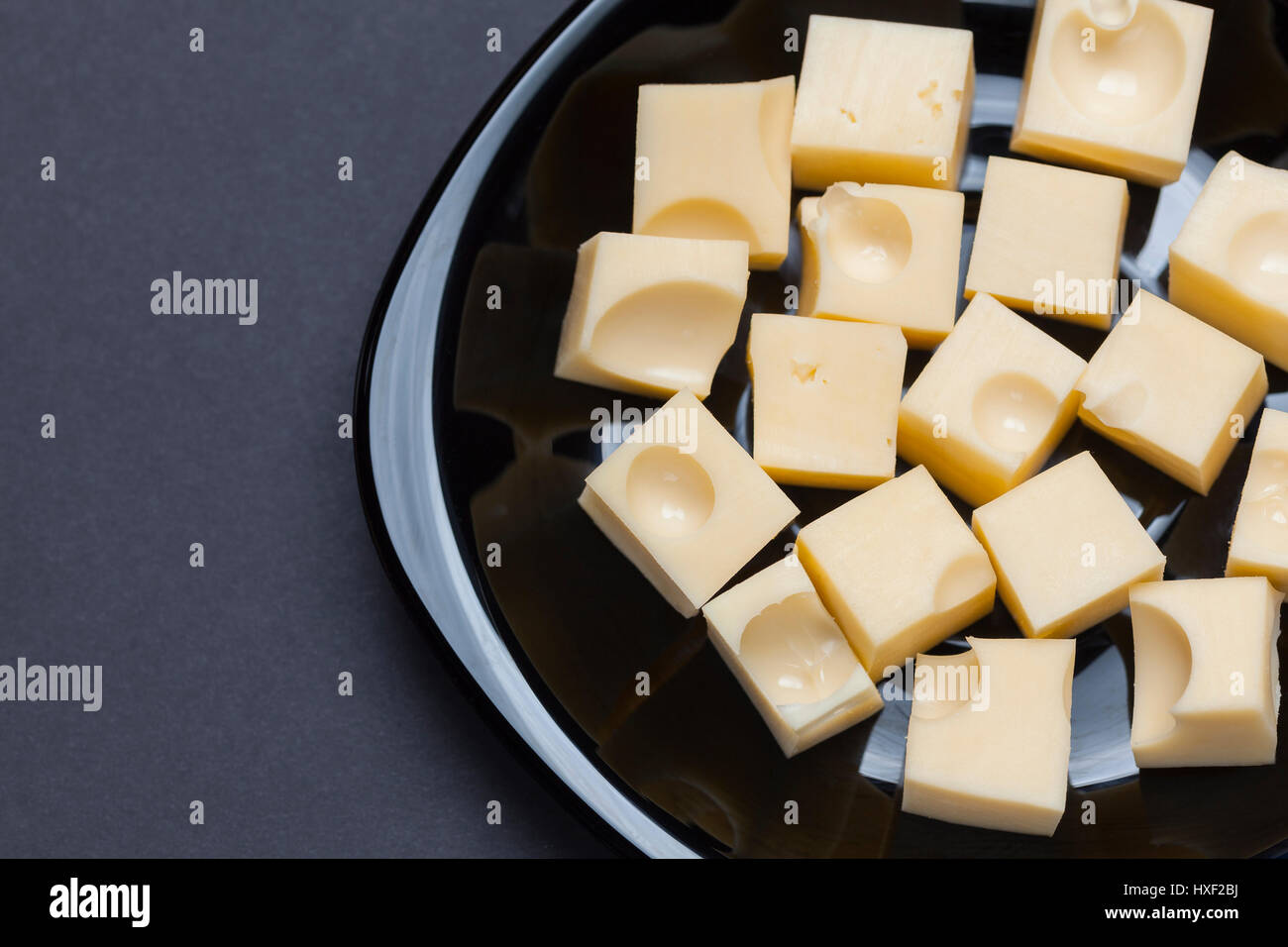 Yellow cheese cubes in a black plate. Close up Stock Photo - Alamy