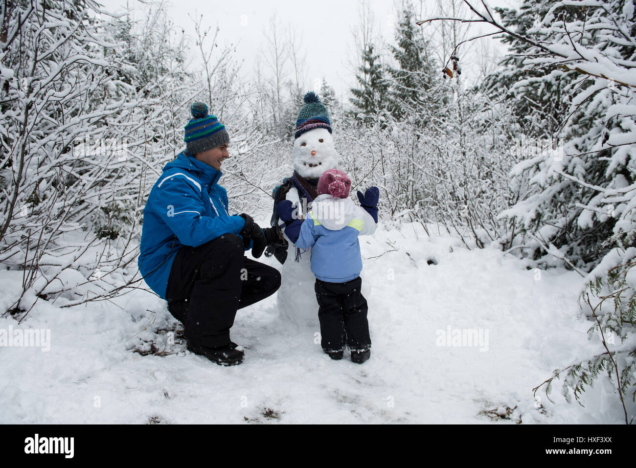 Happy father watching daughter making snowman on beautiful snowy day ...