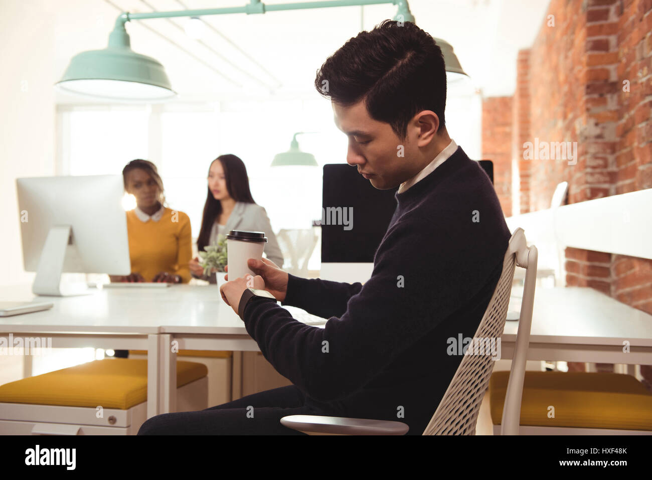 Male executive checking time while having coffee at desk in office ...
