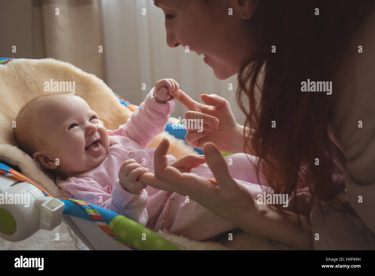 Cheerful mother playing with baby in rocking chair at home Stock Photo ...