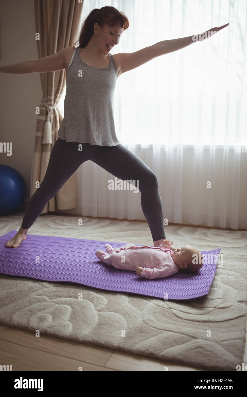 Happy mother doing warrior pose while looking at baby in house Stock ...