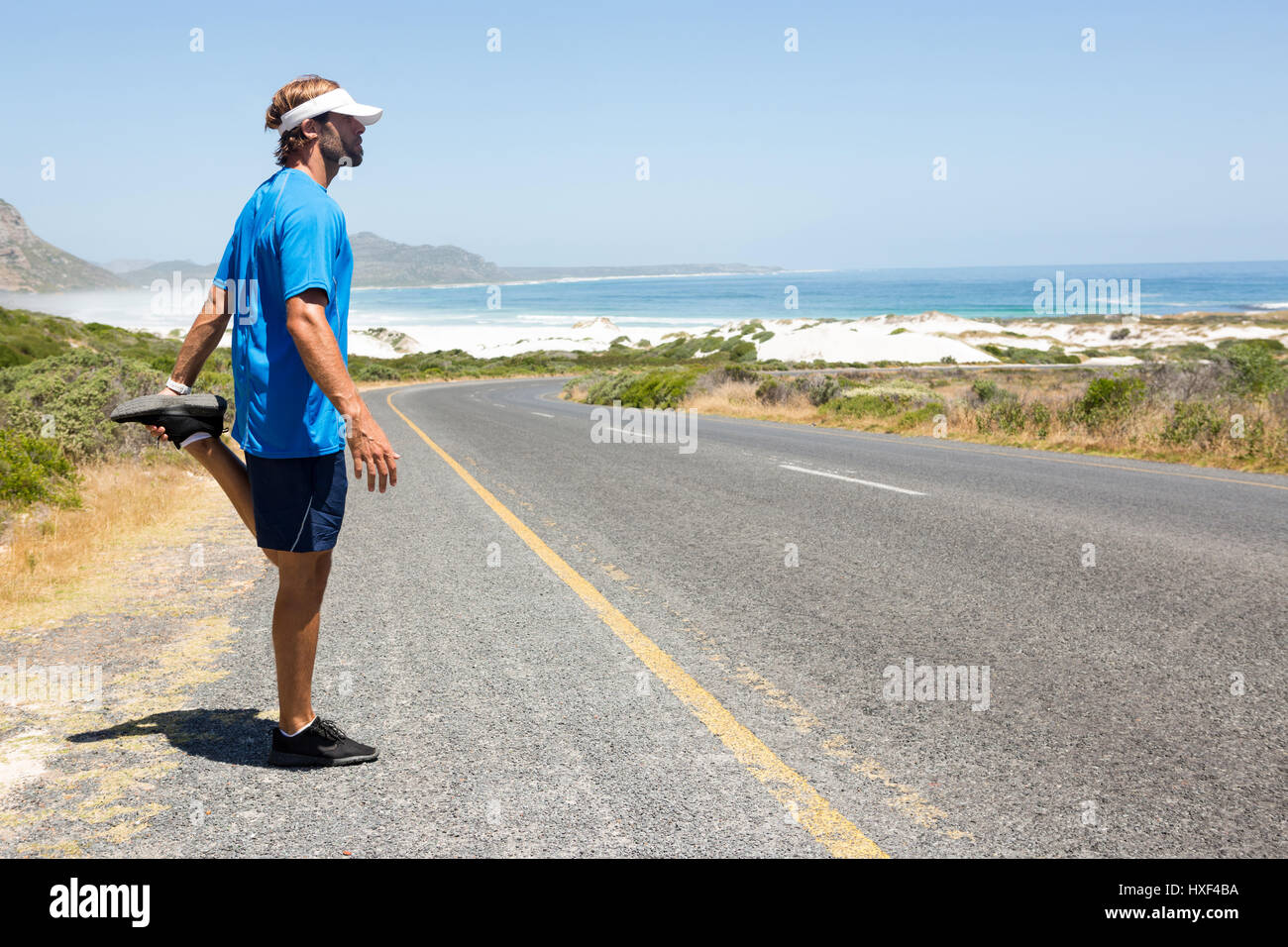 Side view of athlete stretching on roadside Stock Photo - Alamy