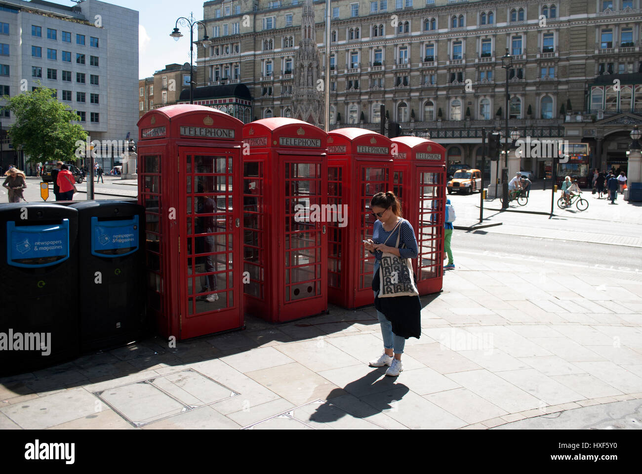 Woman using a mobile phone in front of four red phone boxes in London ...