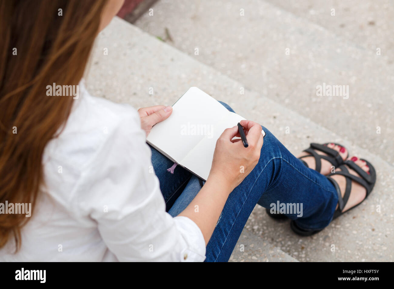 Overhead view of young woman sitting on stairs and making notes in ...