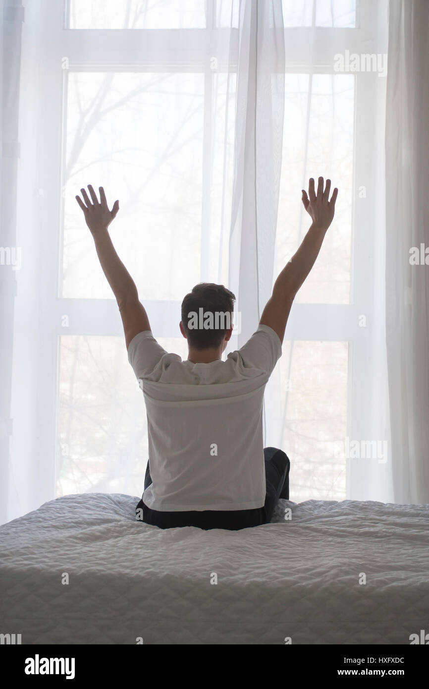 Happy young man stretching in bed after waking up, back view, total ...
