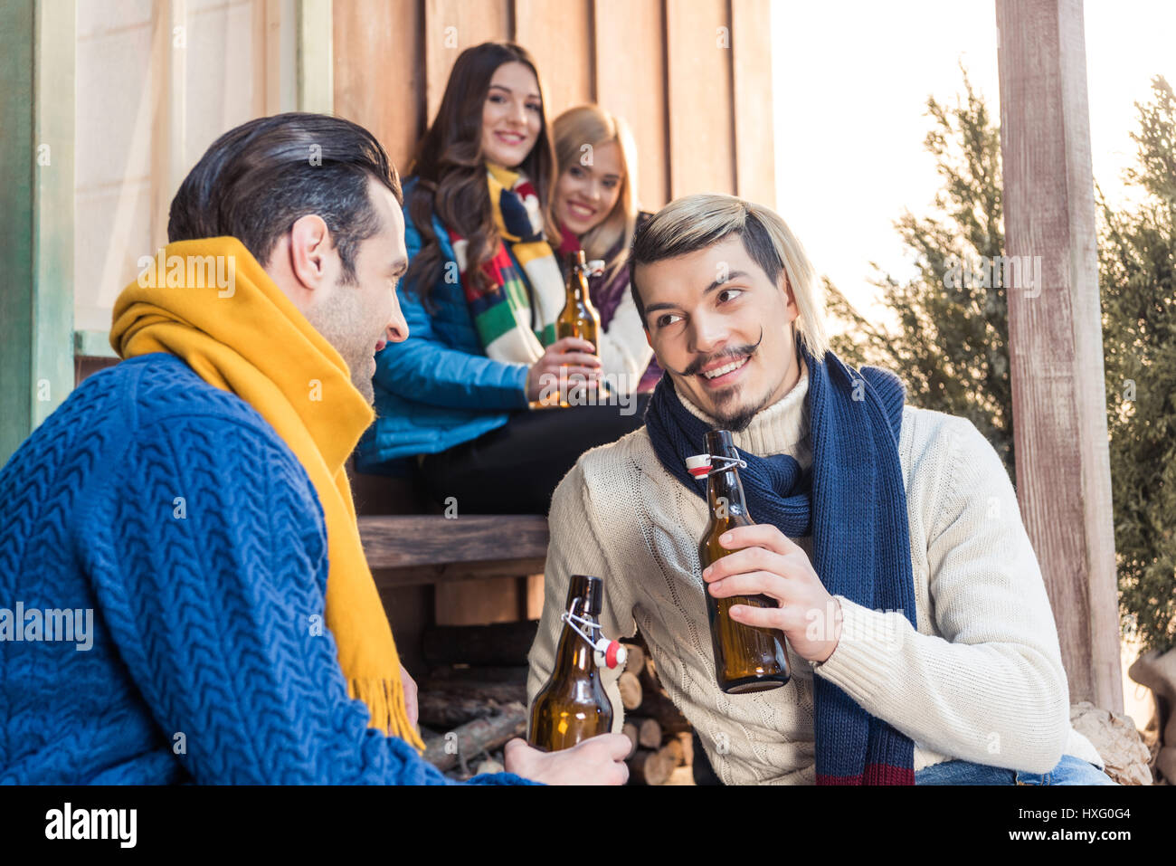 smiling men talking while drinking beer with women looking at them ...