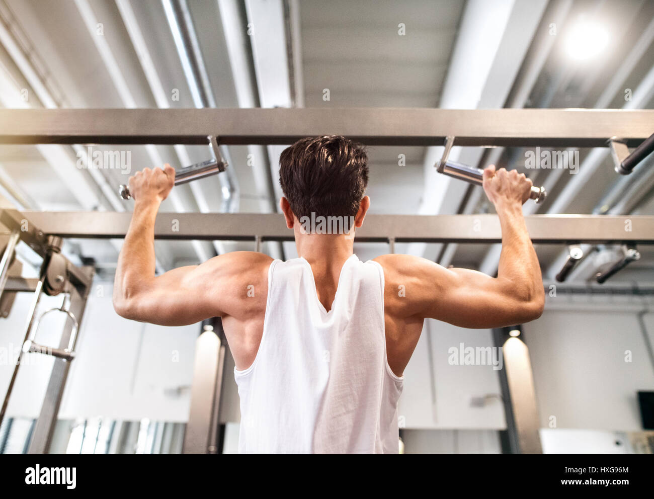 Young hispanic fitness man in gym working out, doing pull-ups on ...