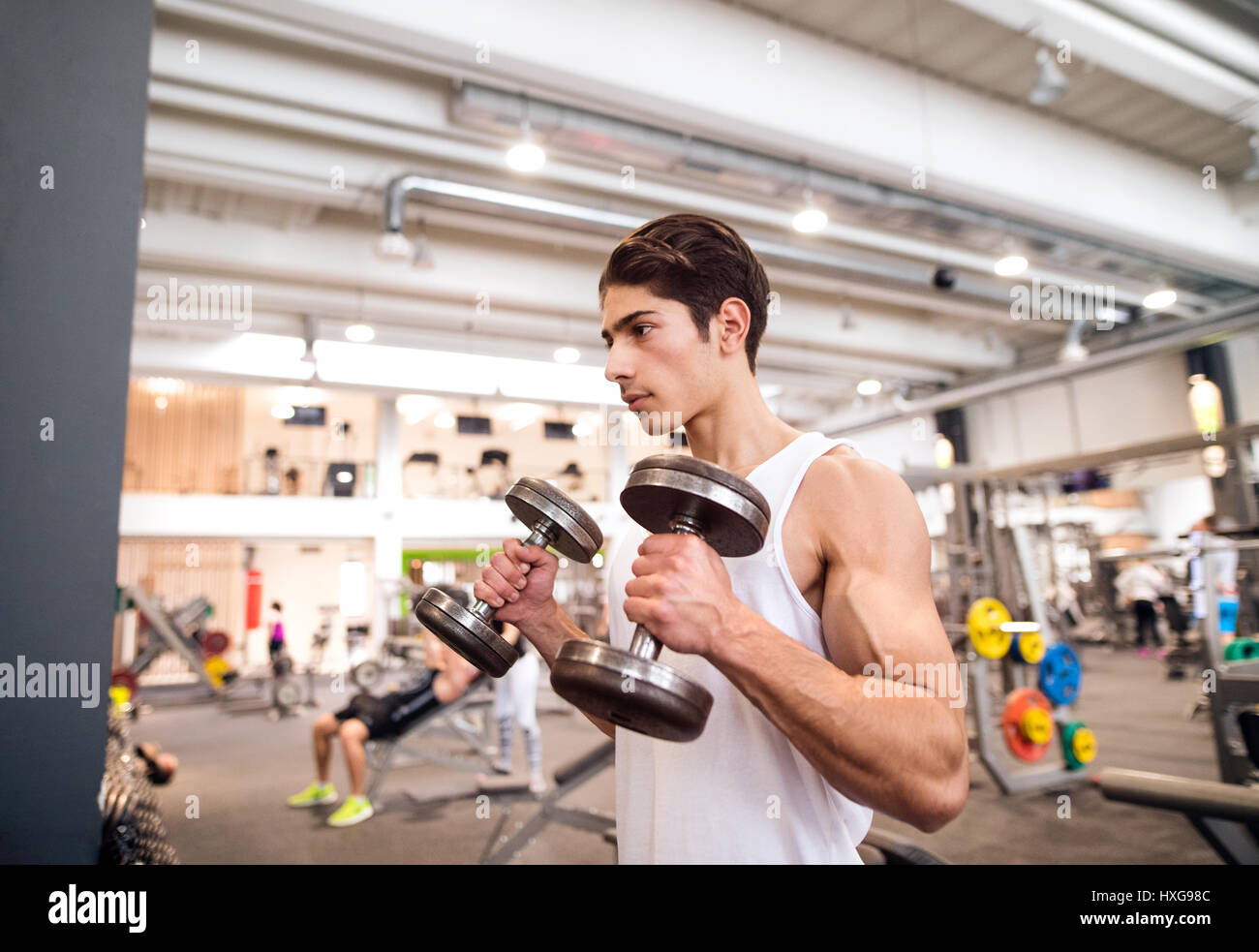 Handsome young hispanic fitness man in gym sitting on bench, working ...