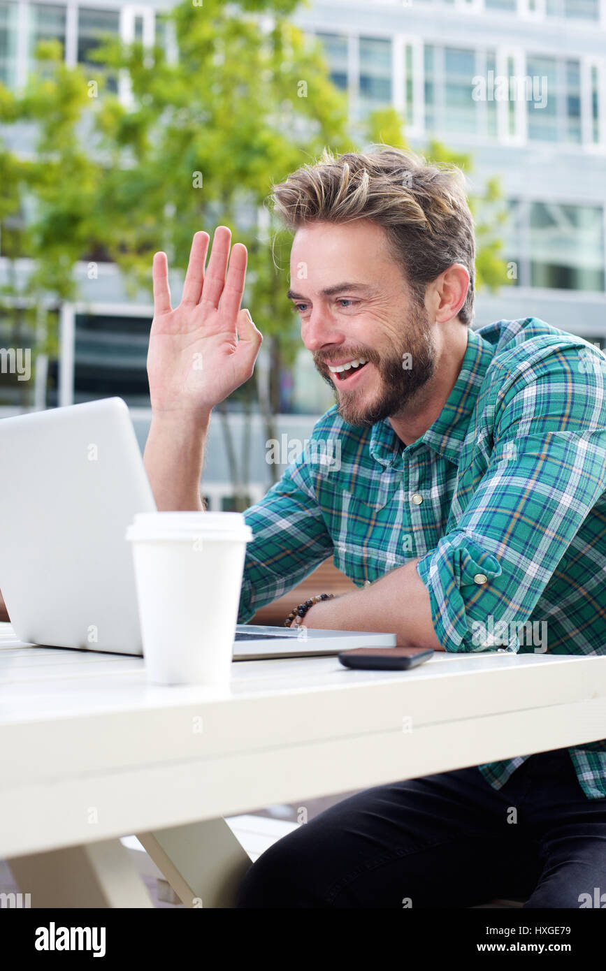 Portrait of a smiling man waving hello on chat with laptop Stock Photo ...