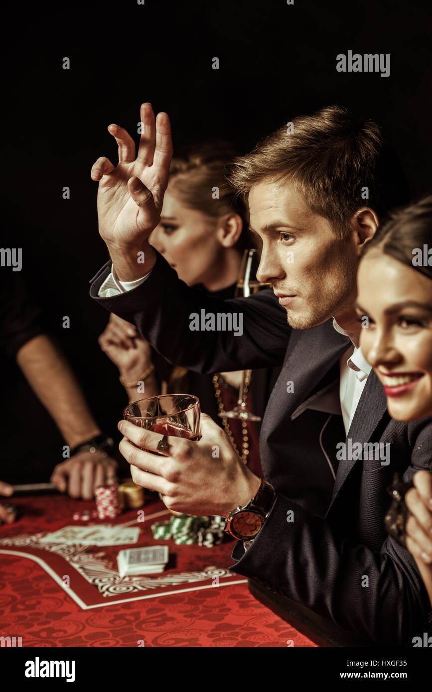 Elegant young smiling people drinking alcohol at poker table on black ...