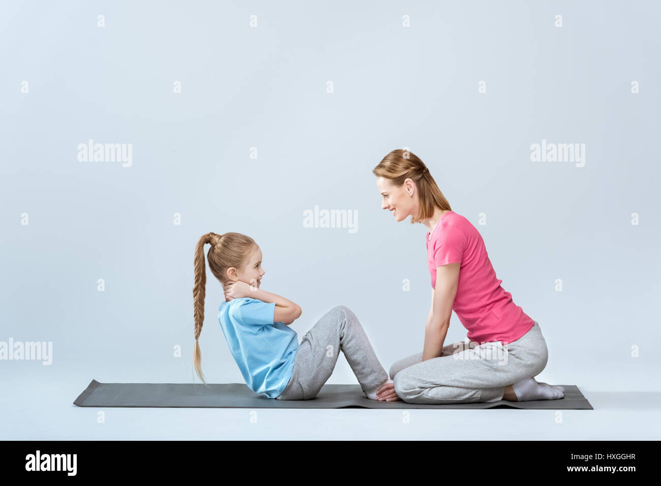 side view of sporty mother and daughter exercising on mats together on ...