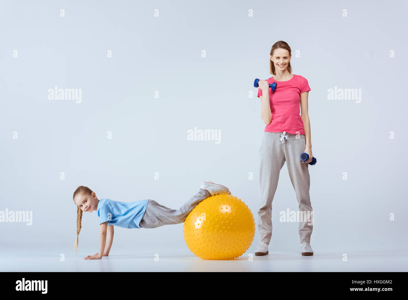 sporty mother with dumbbells and daughter with fitness ball excising ...