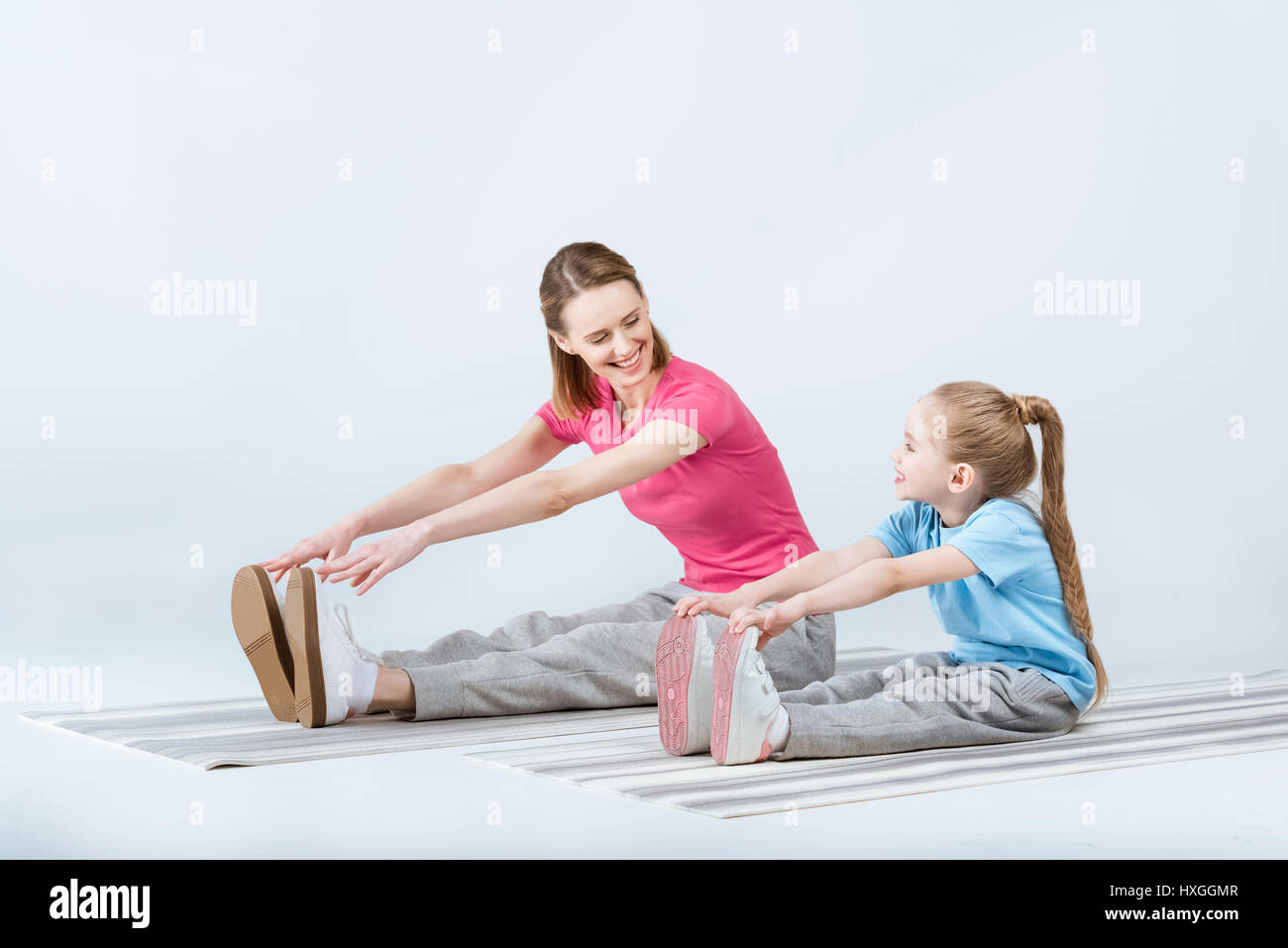 smiling sporty mother and daughter exercising on mats together on white ...