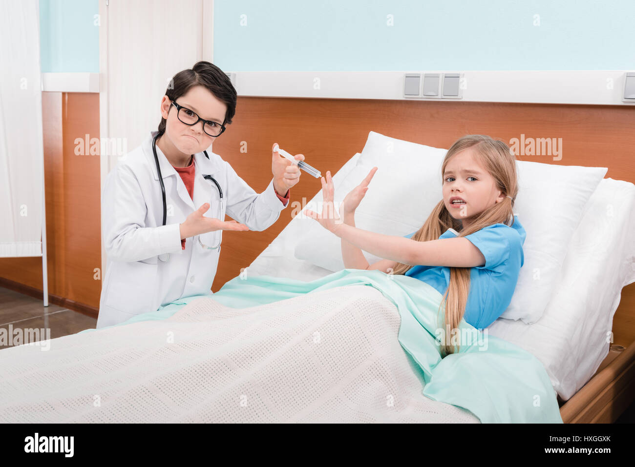 Boy doctor with syringe standing near scared little patient in hospital ...