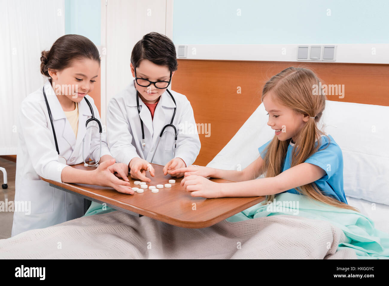 Boy and girl doctors with little patient counting pills on table in ...