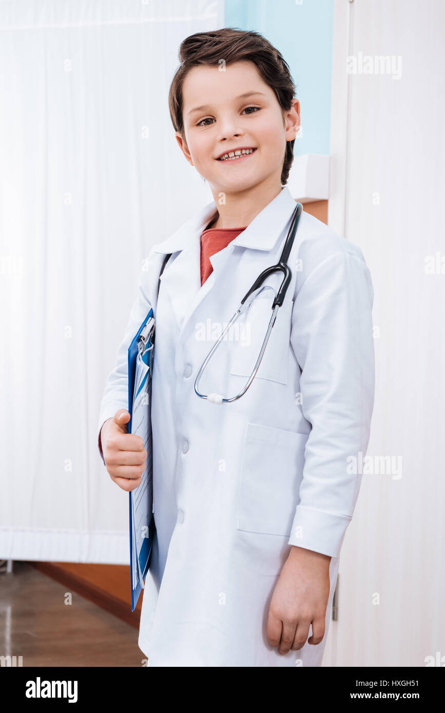Confident boy doctor with stethoscope holding clipboard and smiling at ...