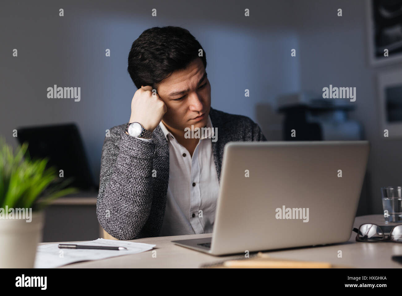 Portrait of sleepy Asian man working overtime alone in dark office late ...