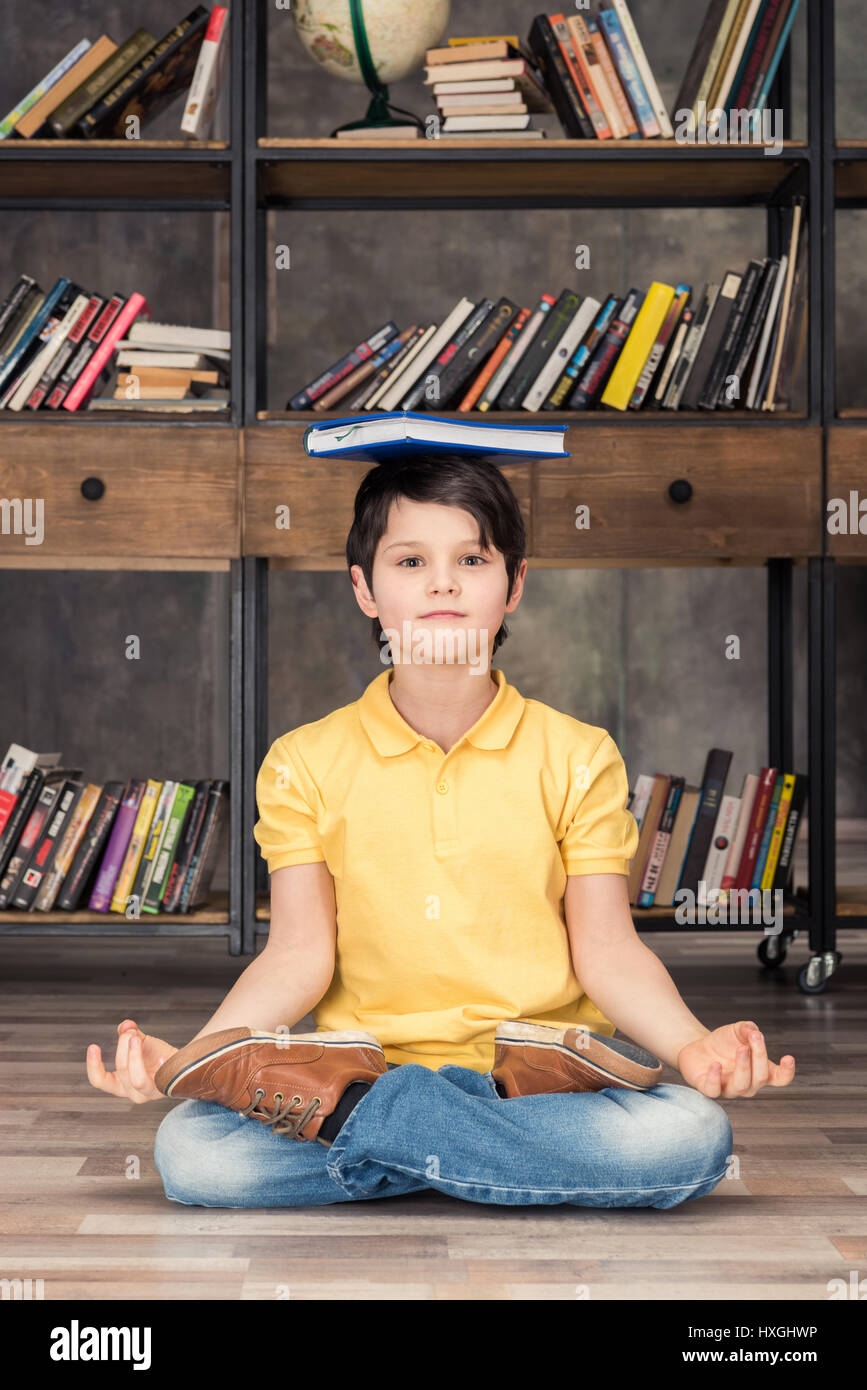 boy with book on head sitting in lotus pose in library Stock Photo - Alamy
