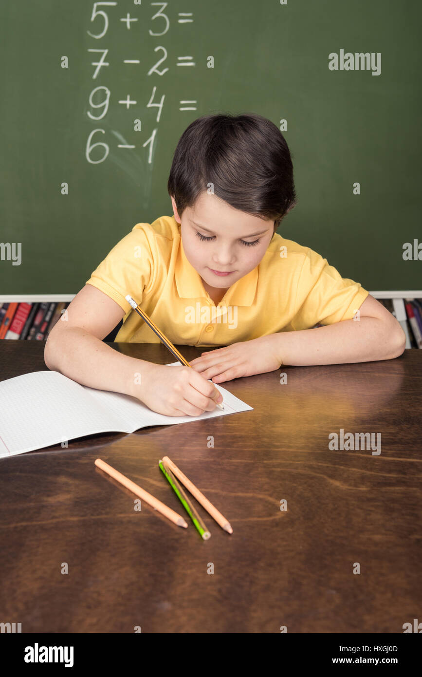 portrait of focused boy writing in copybook in classroom Stock Photo ...