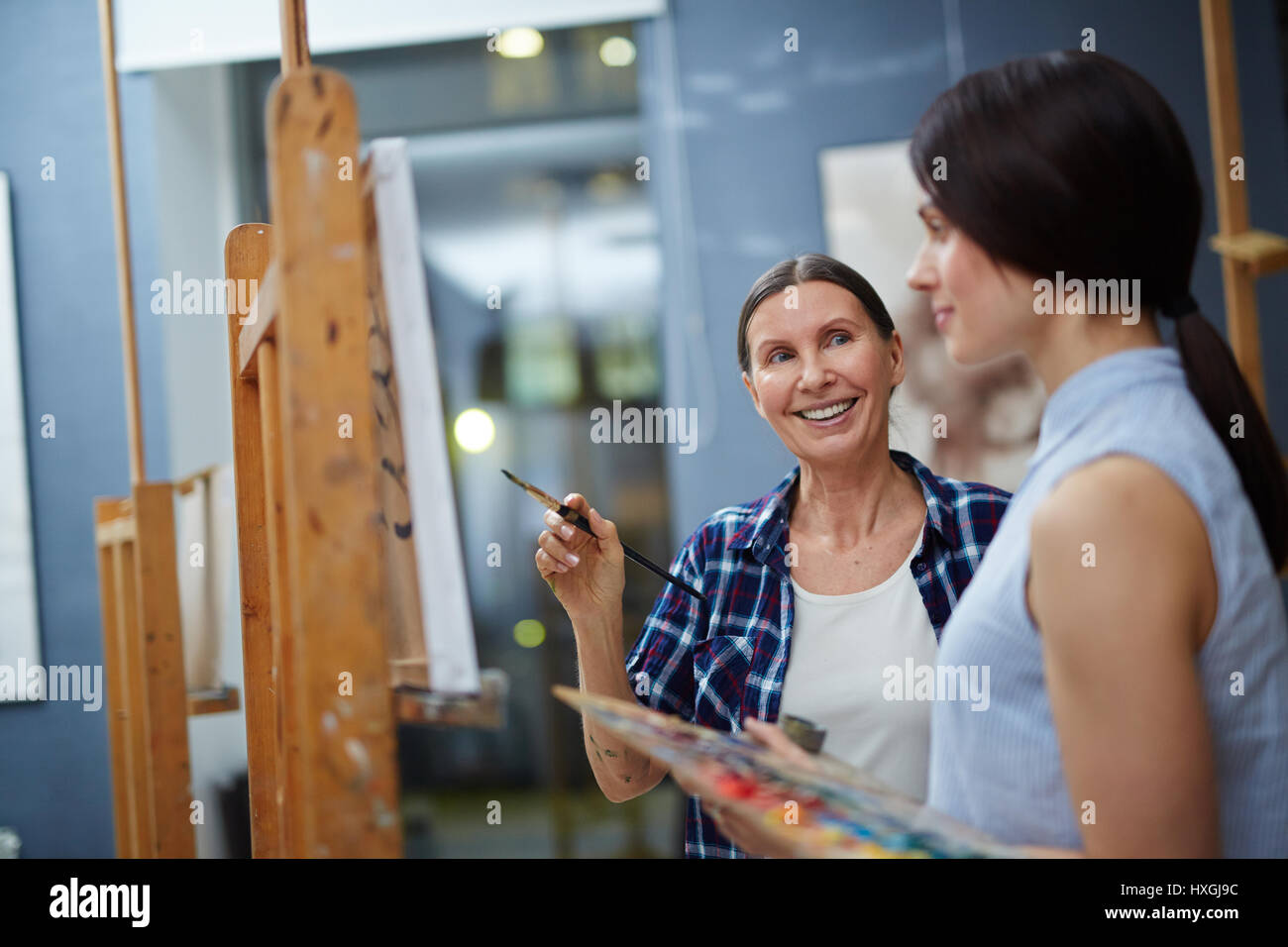 Happy teacher of arts talking to young student about her painting on ...