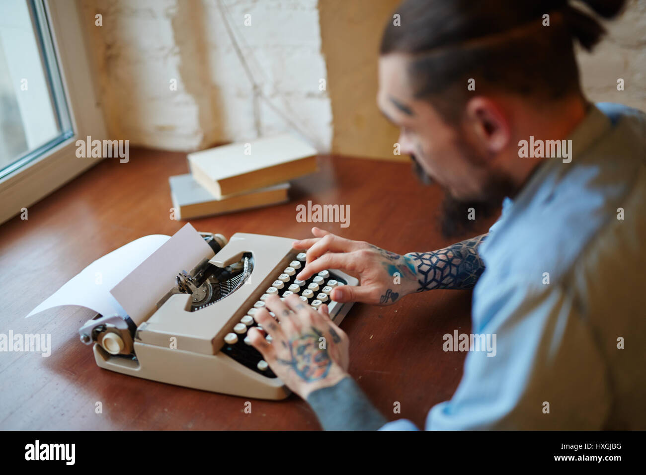 Portrait of creative tattooed man using old-school vintage typewriter ...