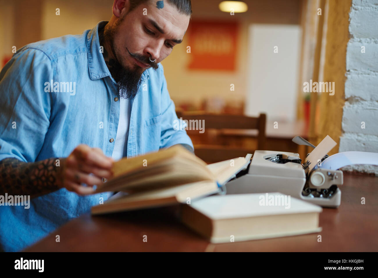 Portrait of stylish creative man with tattoos and beard turning pages ...