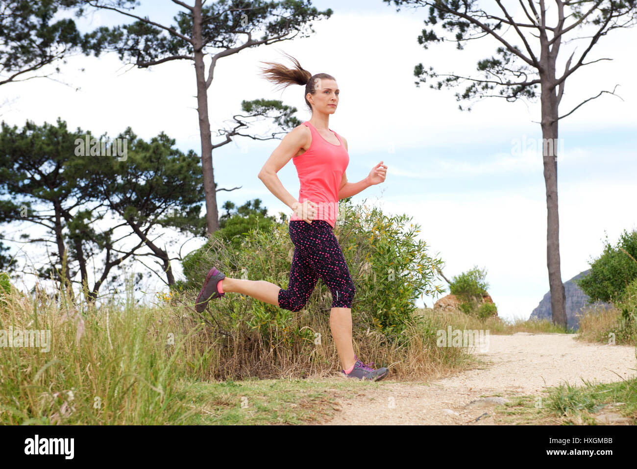 Full length portrait of sporty woman running on dirt path outdoors ...
