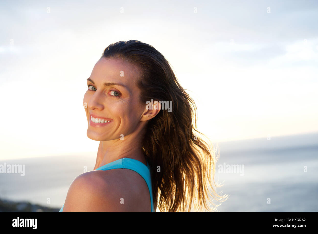 Close up portrait of woman looking over shoulder with sea in background ...