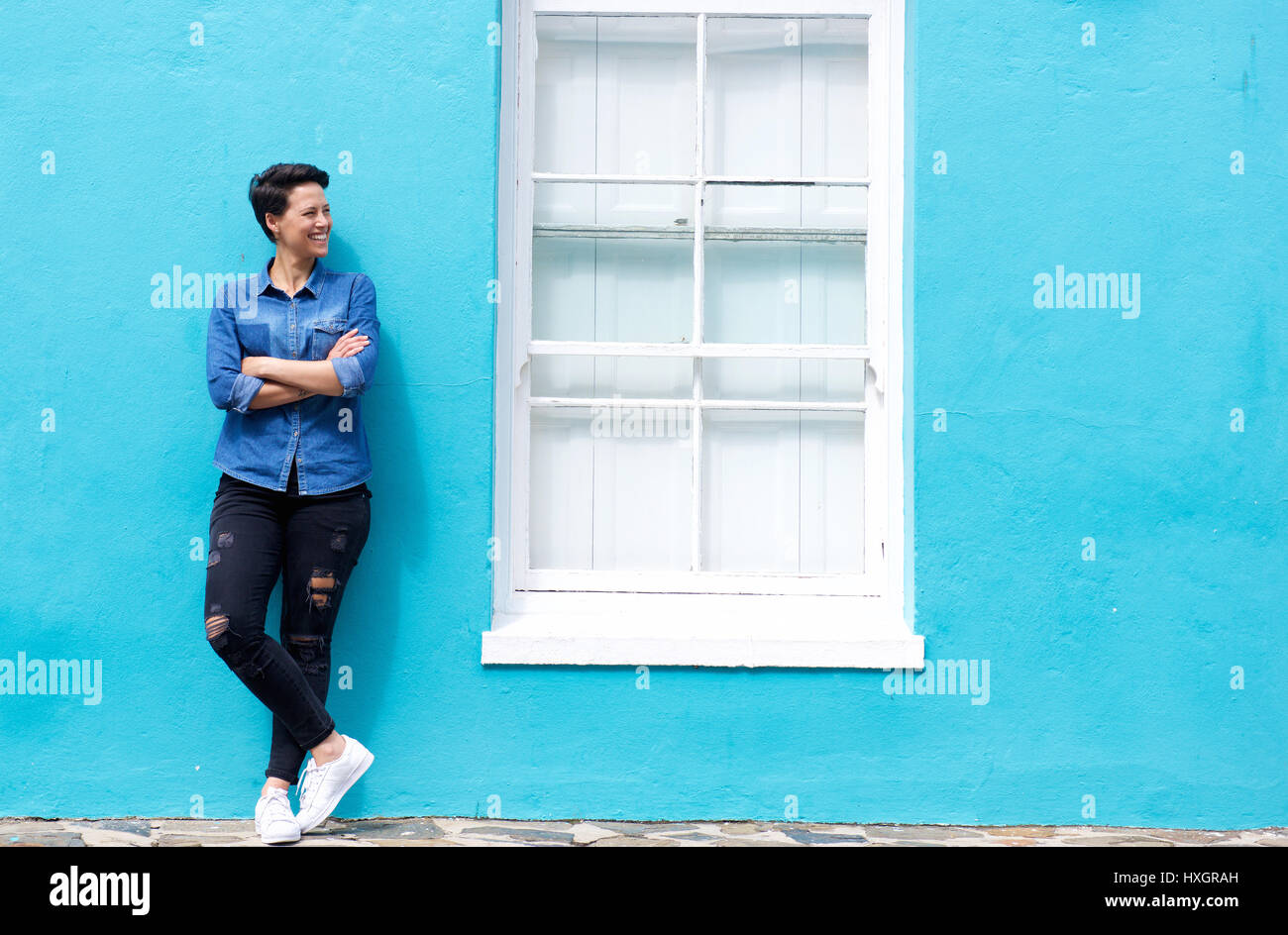 Full length portrait of a happy young woman standing next to window ...