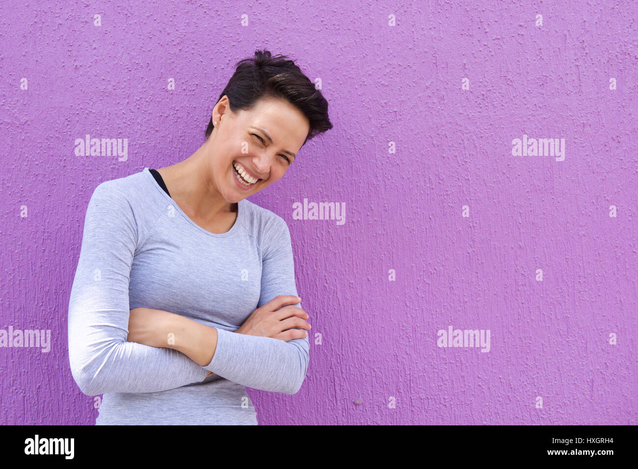 Portrait of a young woman laughing with arms crossed on purple ...