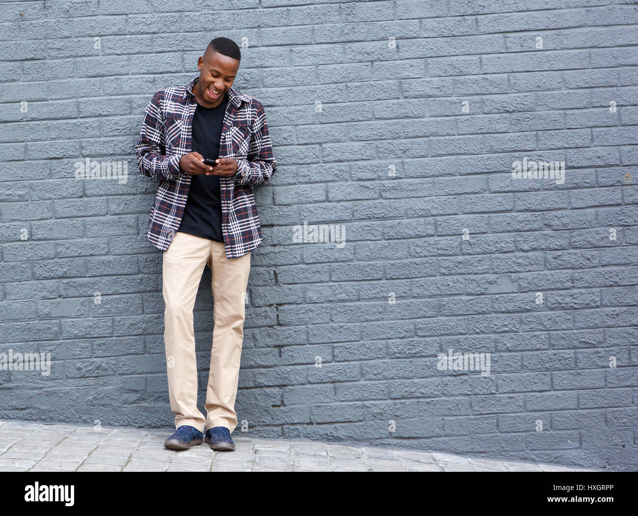 Full length portrait of cool young man standing against a gray wall and ...