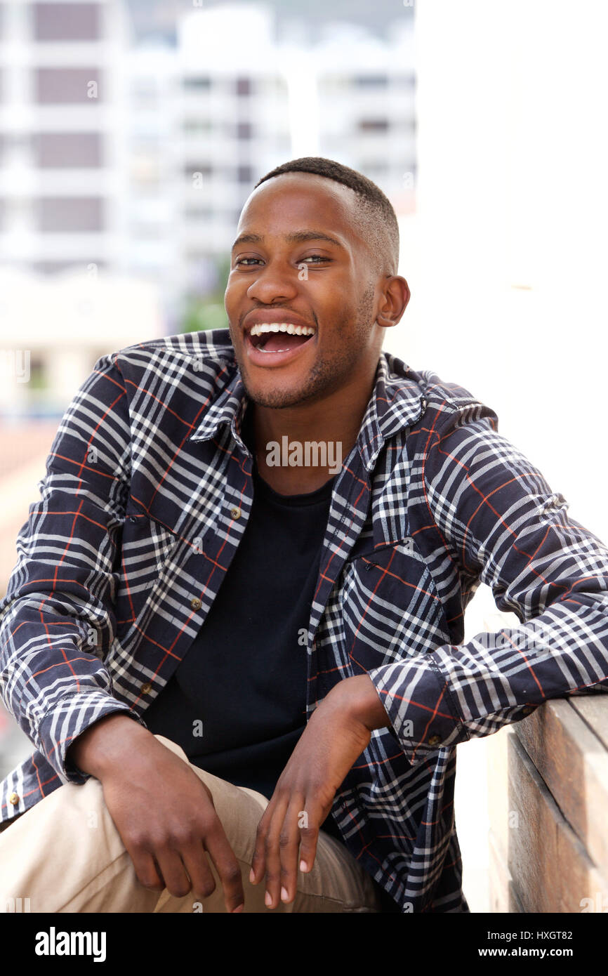 Portrait of smiling young african man sitting on a bench outdoors Stock ...