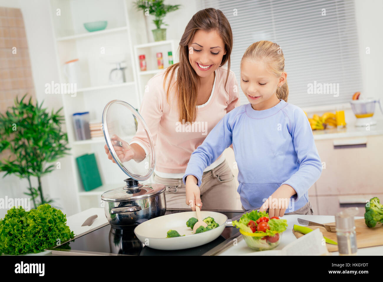 Young beautiful mother and her cute daughter cooking healthy meal in ...