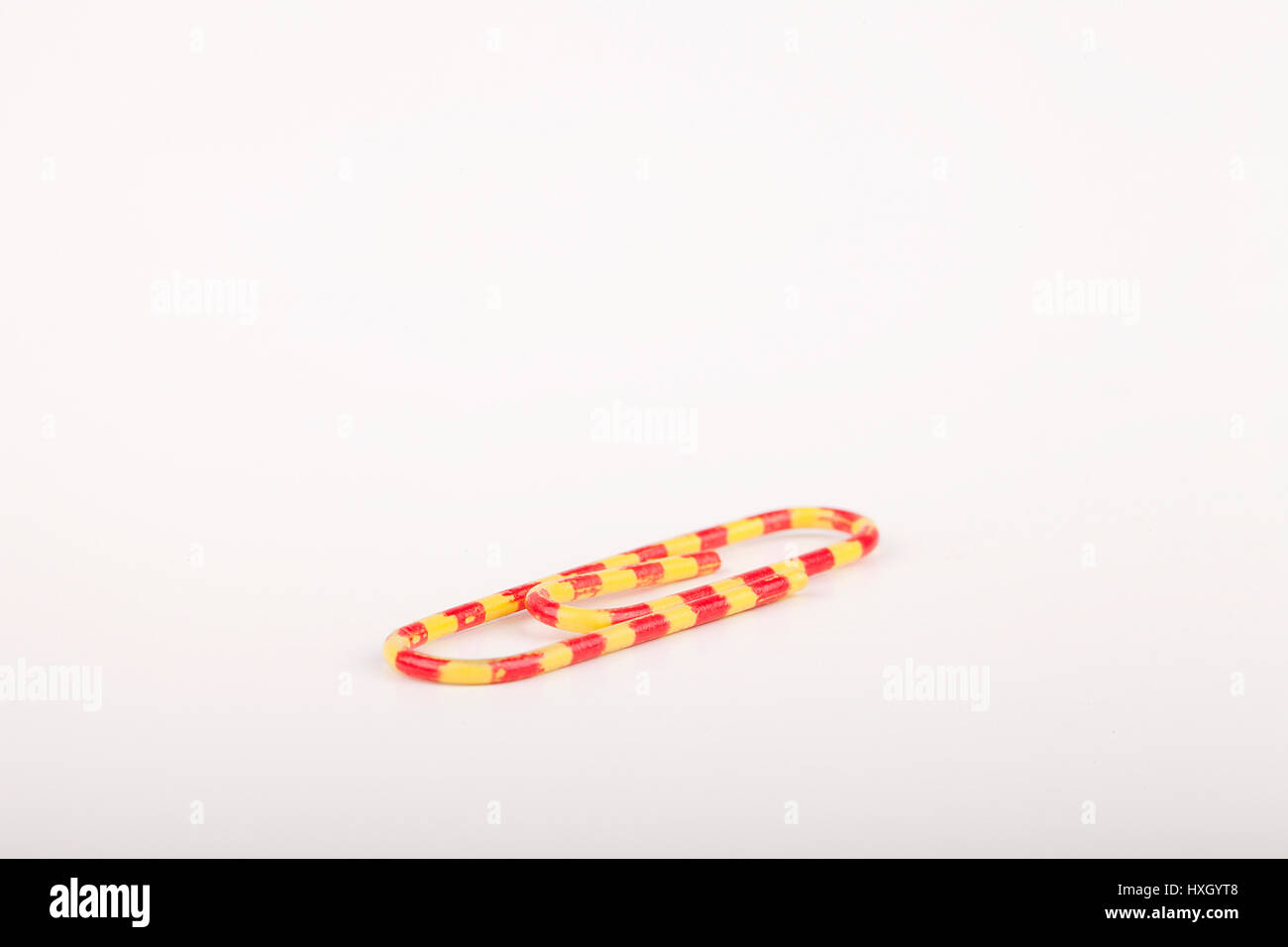 Red and yellow paper clip on a white surface. Paperclip isolated on ...